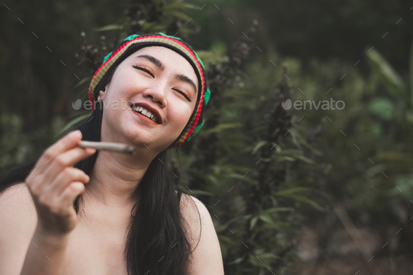 Yong Asia woman smoking marijuana at cannabis tree plant background Stock Photo by thichaa